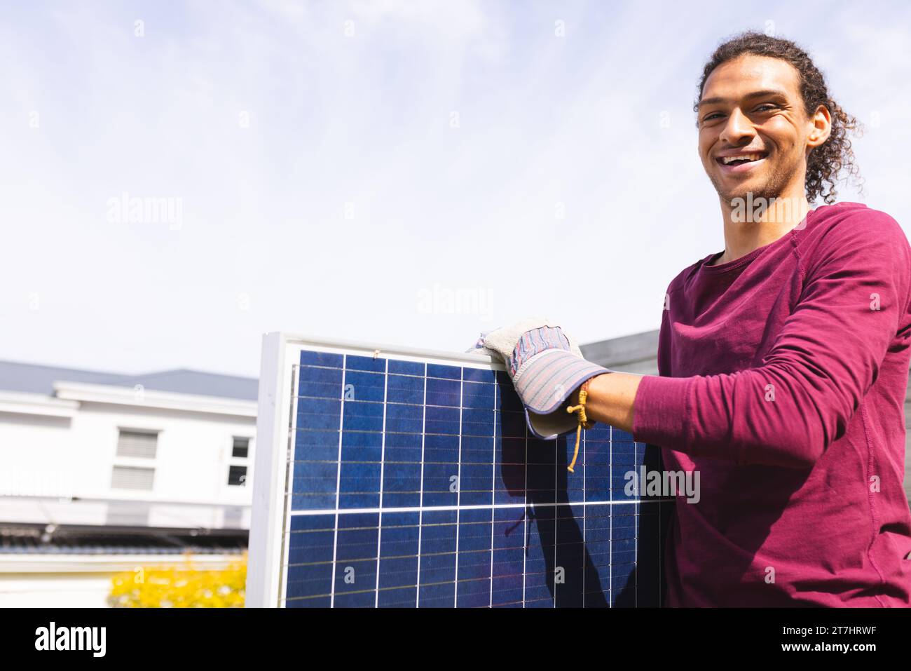 Happy biracial man carrying solar panel and smiling in sunny garden ...
