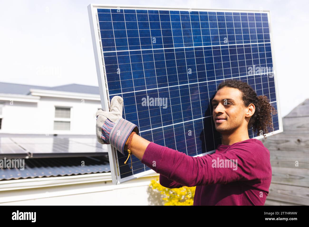 Happy biracial man carrying solar panel and smiling in sunny garden ...
