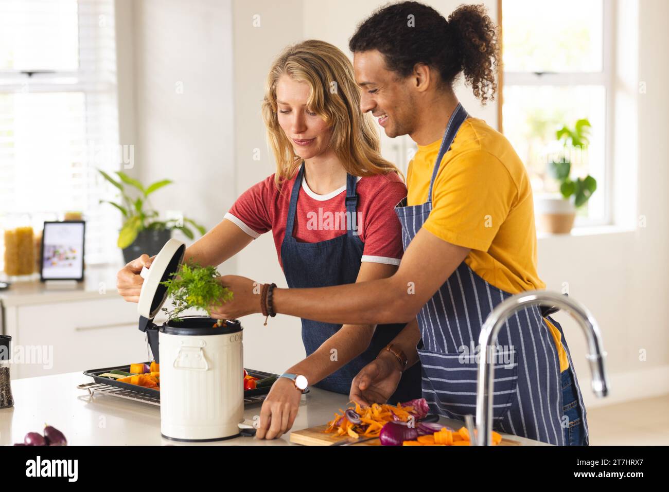 Happy diverse couple composting vegetable waste in sunny kitchen at ...