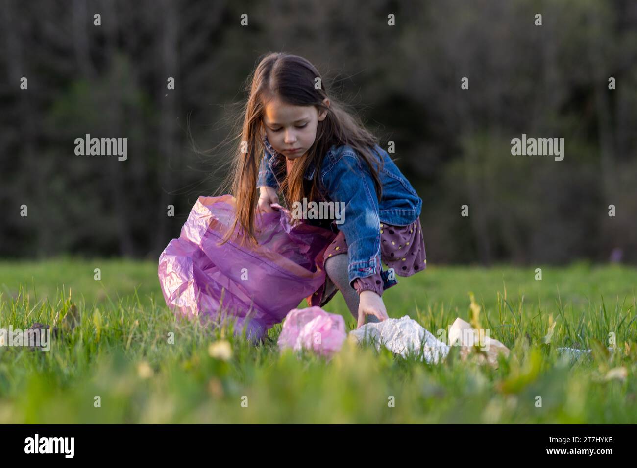 Lovely little girl with long hair in denim jacket collects garbage in ...