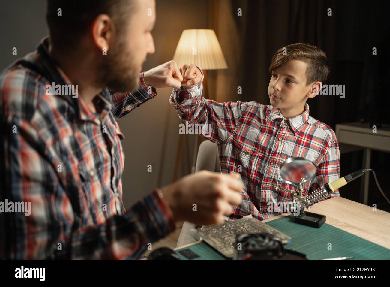Father and son soldering circuit board with soldering iron at home ...