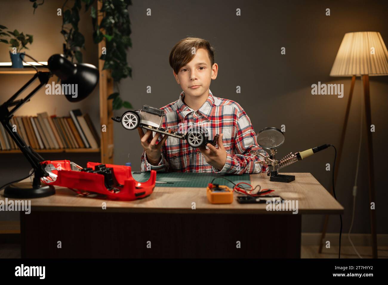 Portrait of teen boy fixing and soldering remote controlled red car ...