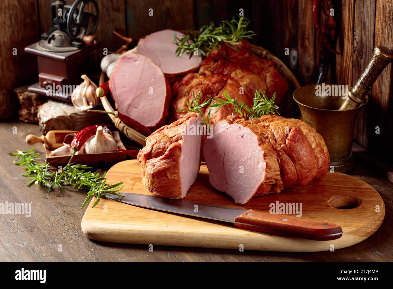 Smoked ham with herbs, spices, and kitchen utensils on an old wooden ...