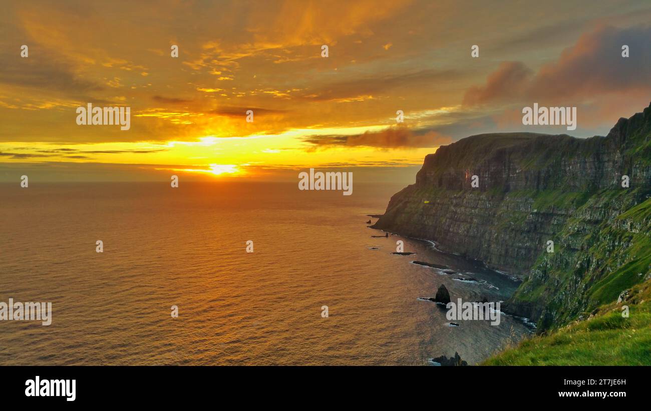A dramatic scene of a golden sunset over a body of water and cliffs ...