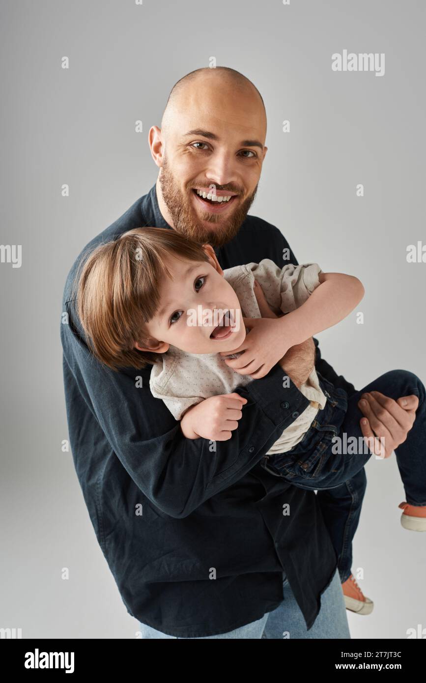vertical shot of joyous father holding his cheerful son and looking ...