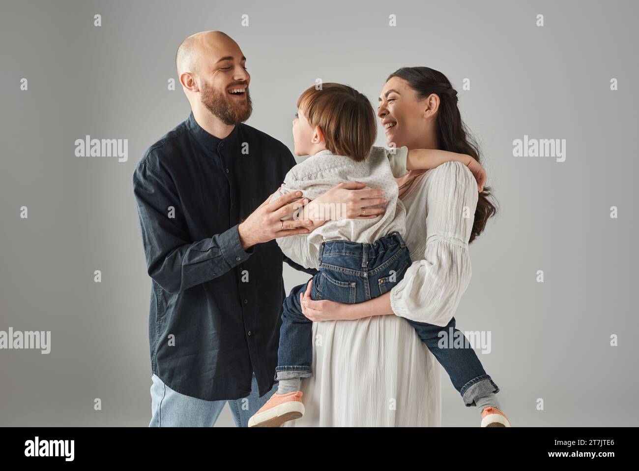 happy modern parents in classy outfits holding their little son on gray ...