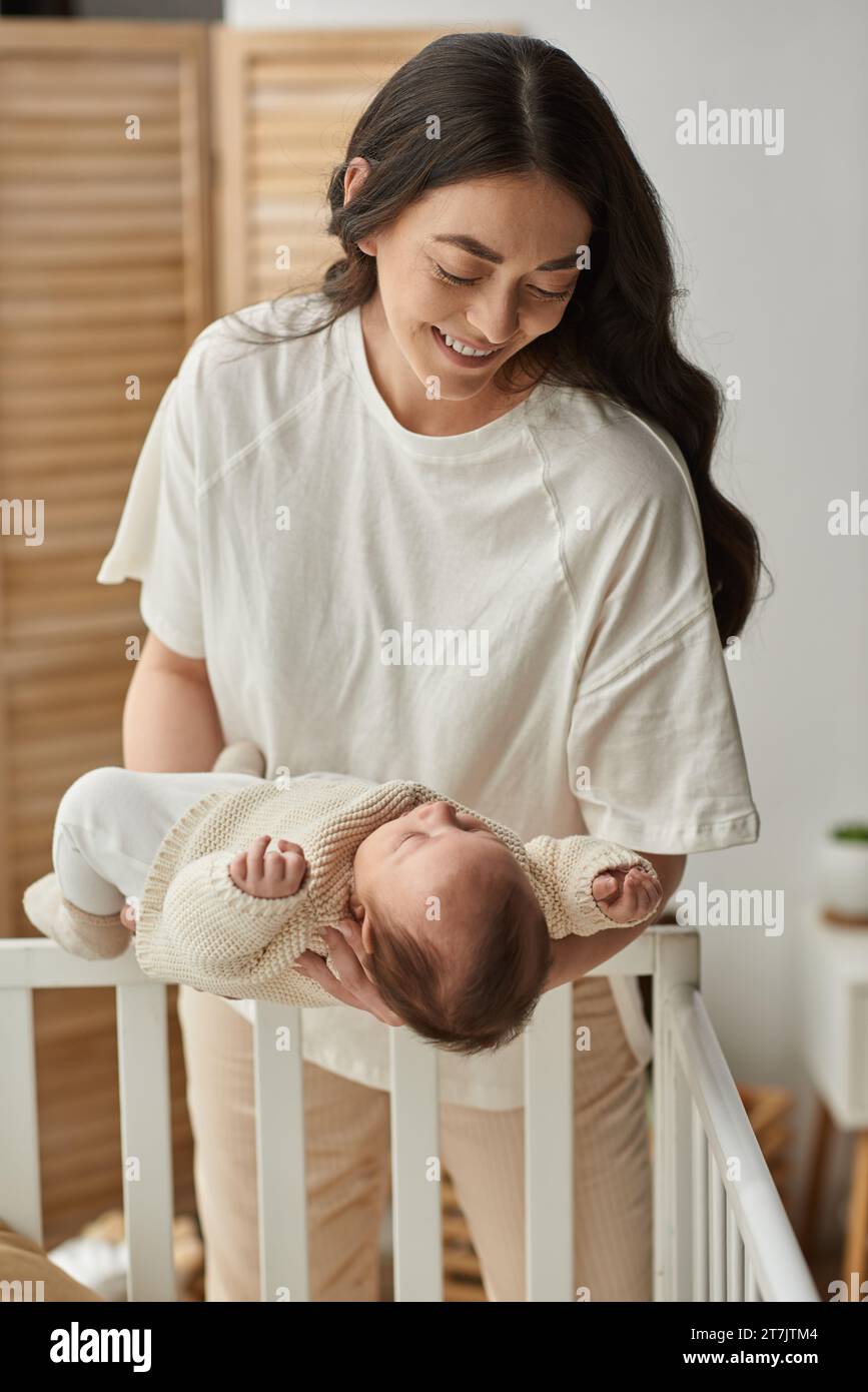 vertical shot of happy modern mother putting her cute newborn baby into ...