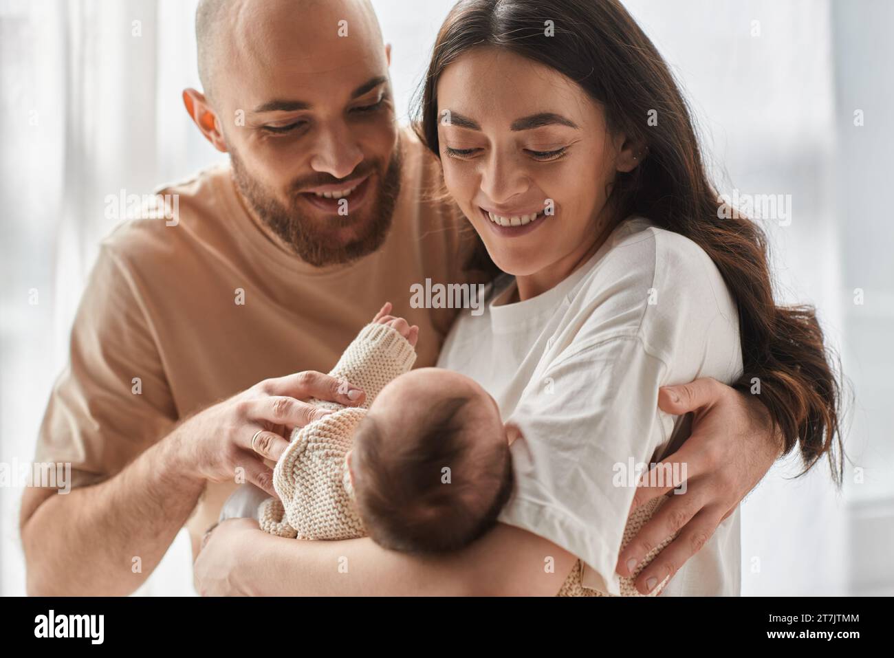 joyous happy parents in cozy homewear smiling happily at their newborn ...
