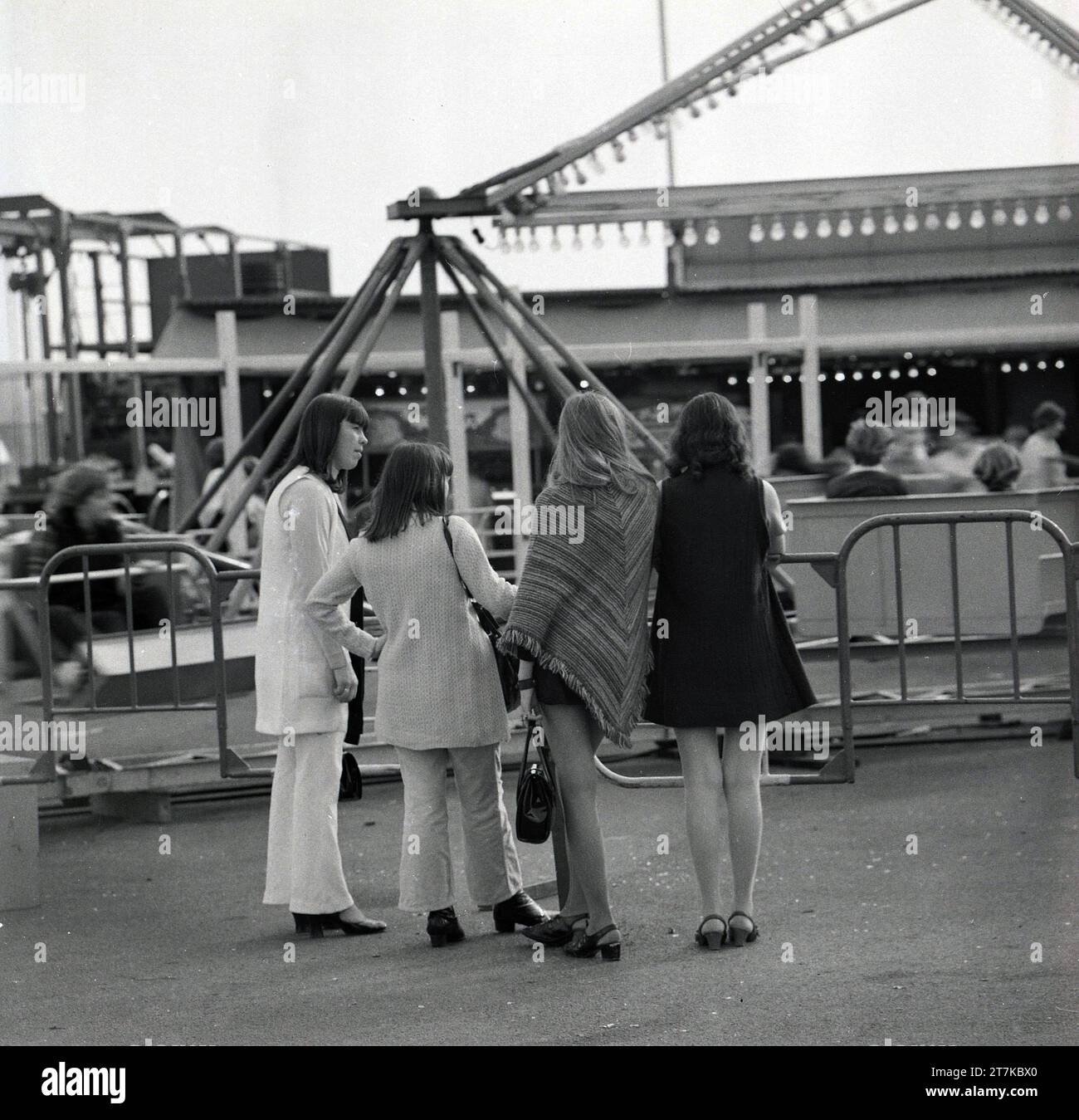 1970s, four young women at a fairground, standing together, watching ...