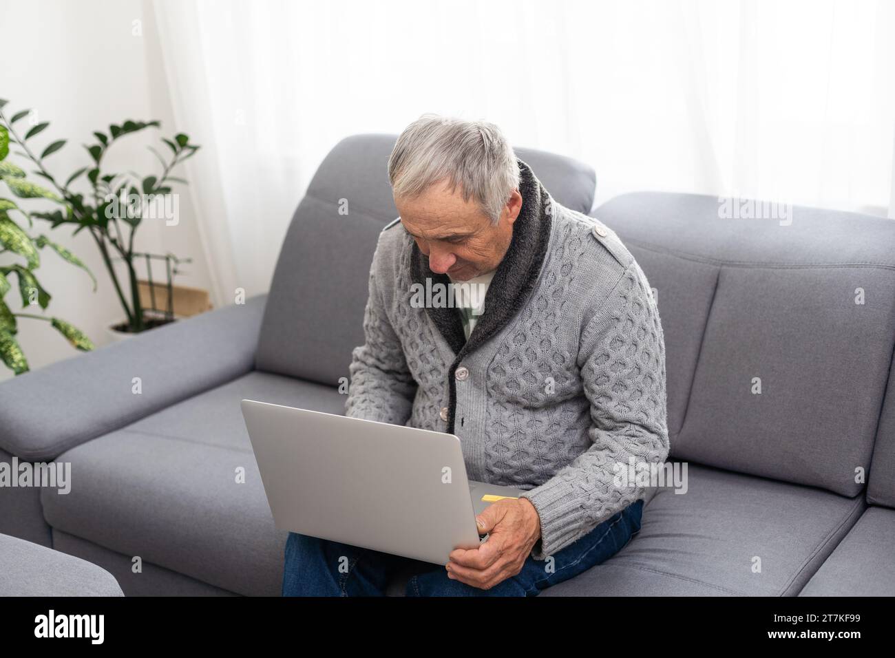 Older man sitting on sofa, smiling at computer screen at home Stock ...