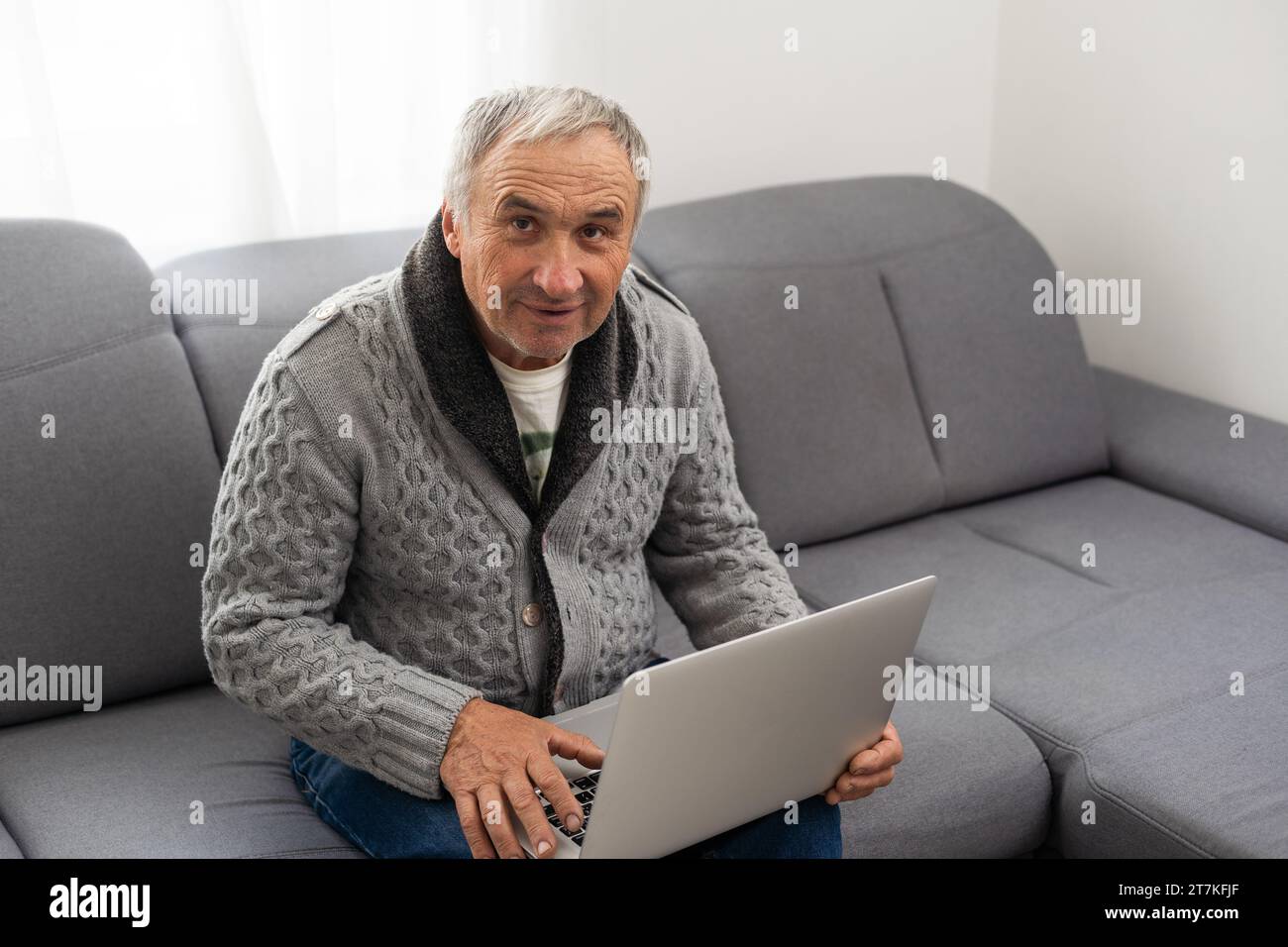 Older man sitting on sofa, smiling at computer screen at home Stock ...