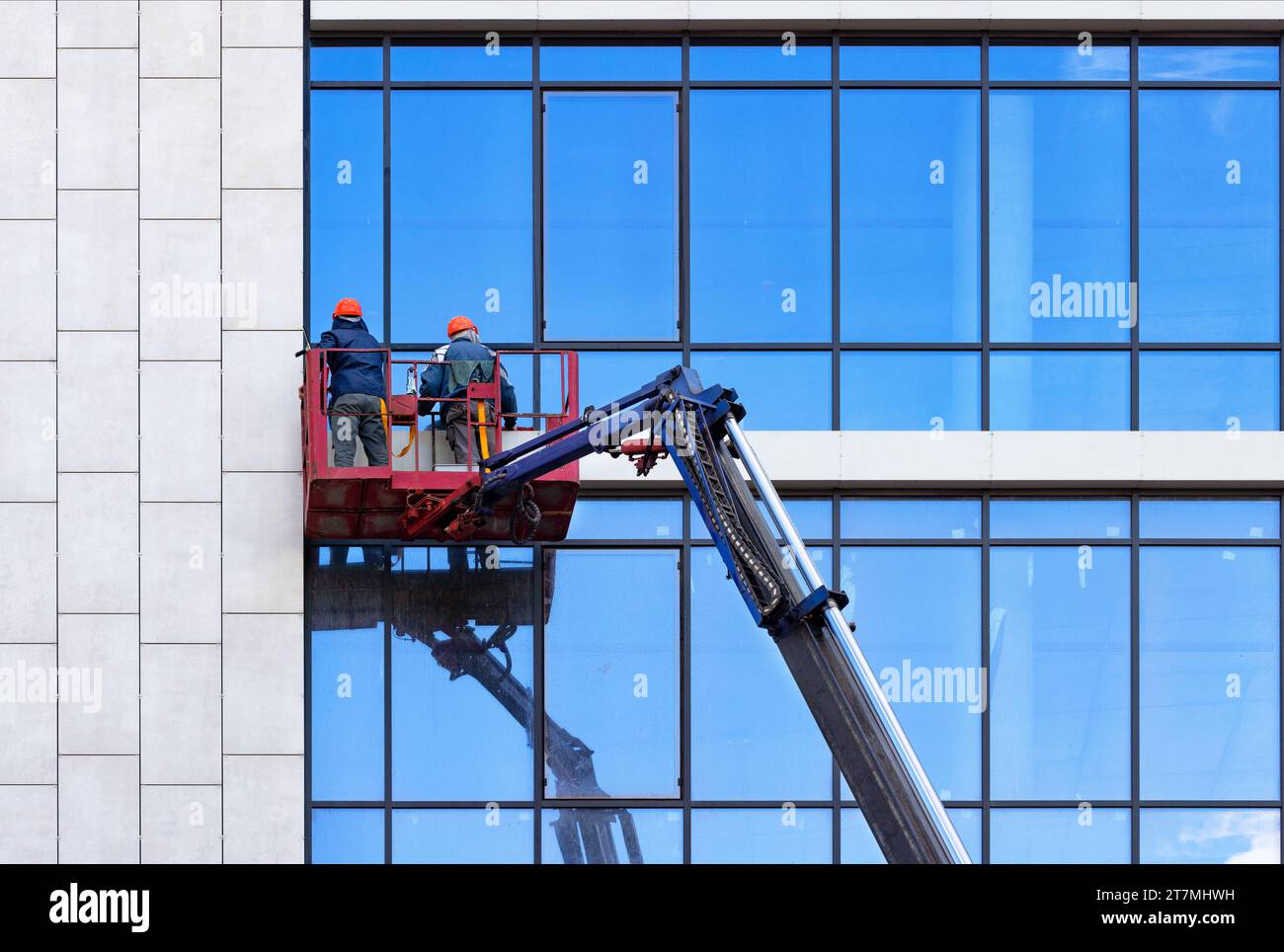 Workers wash glass windows of an office building in a crane bucket ...