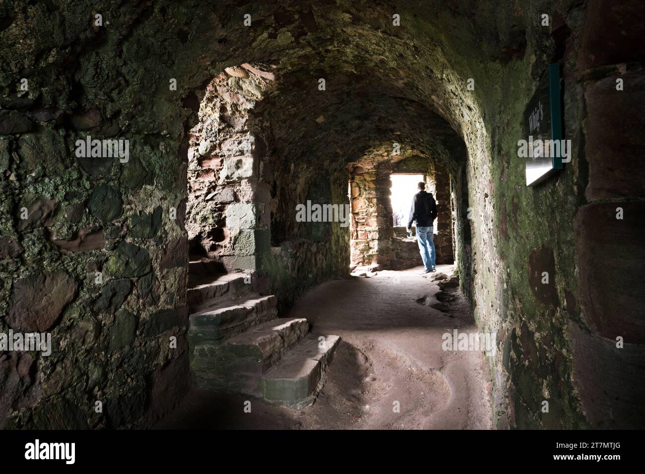 An adult man explores an old abandoned stone ruin with a curved ceiling ...