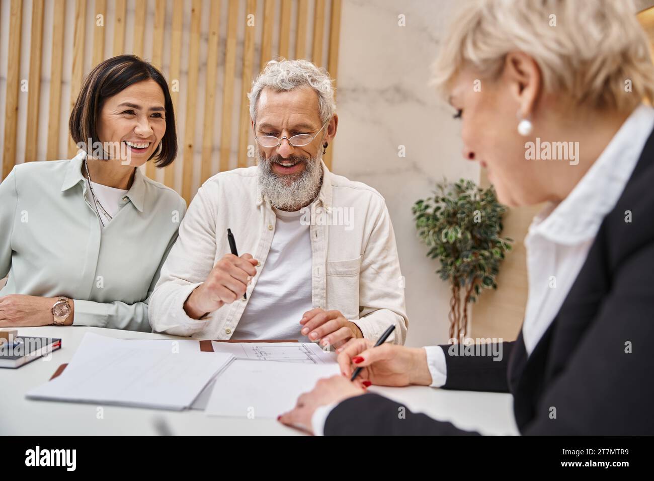 happy middle aged realtor signing contact near married couple in real ...