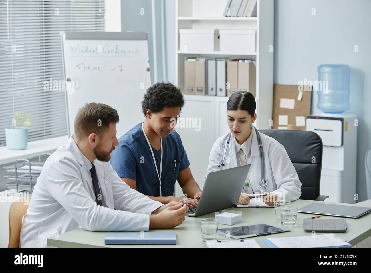 Diverse group of three young doctors looking at computer screen while ...