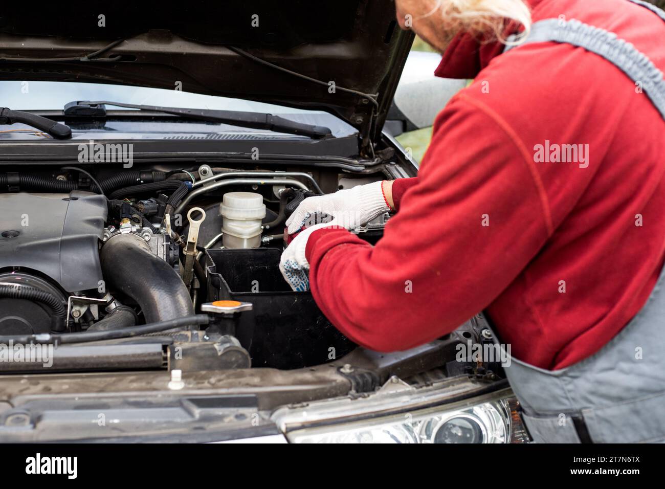 A man under the hood of a car is doing repairs and installing a battery ...