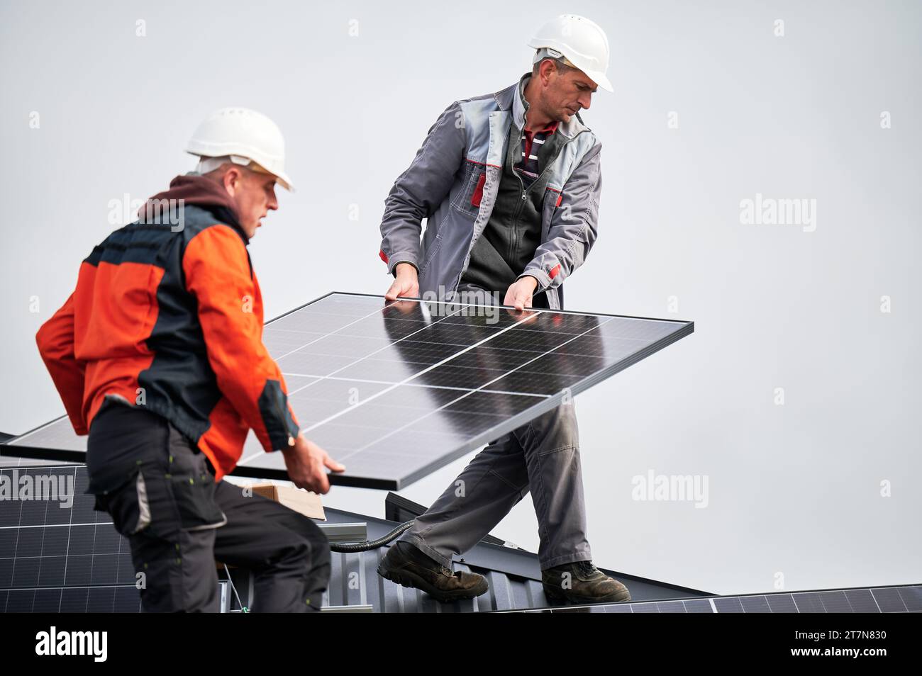 Technicians installing solar panel system on roof of house. Men workers in helmets carrying ...