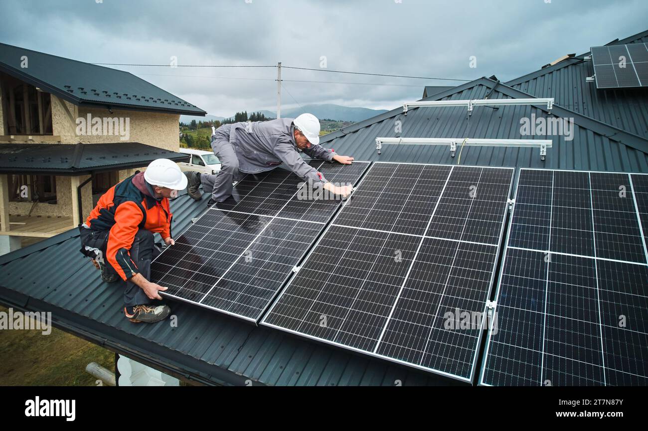 Workers installing photovoltaic solar panels on roof of house. Men ...