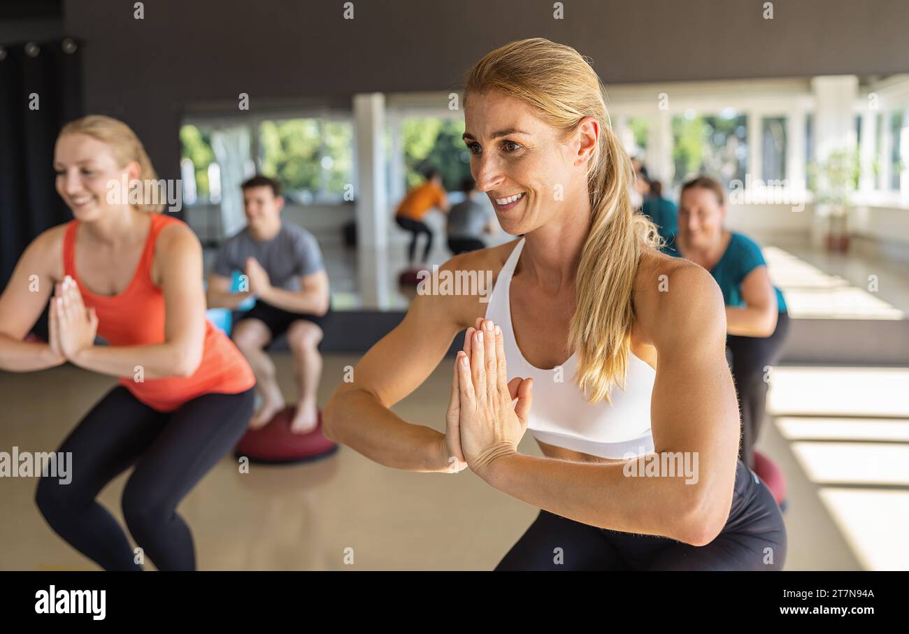 Woman in fitness class performing squats with hands together at a ...