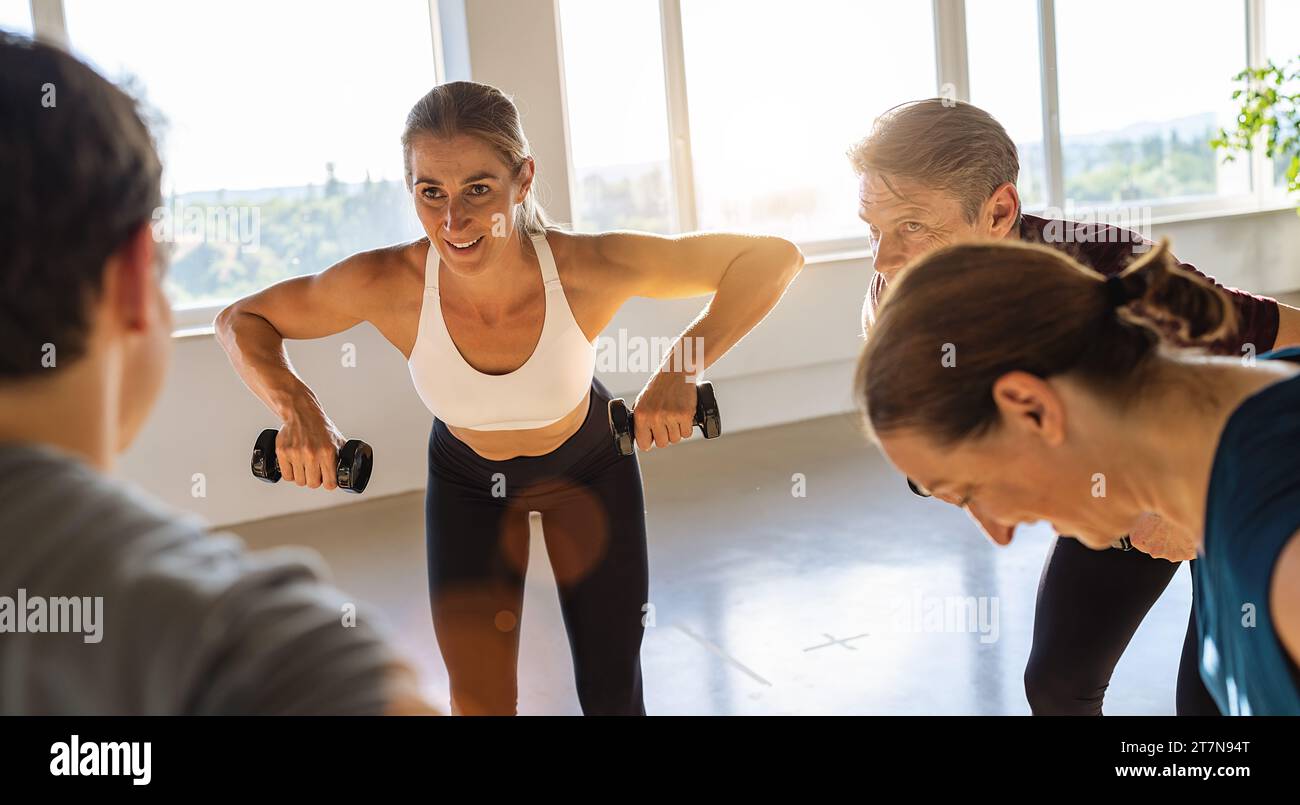 Intense group workout with dumbbells, focused faces, large windows in ...