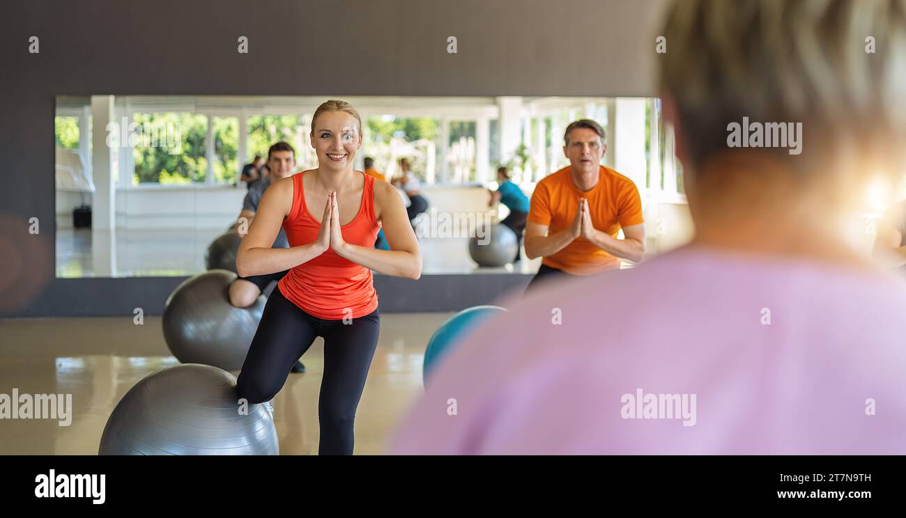 smiling woman flexing leg muscles with exercise ball in gym and folding ...