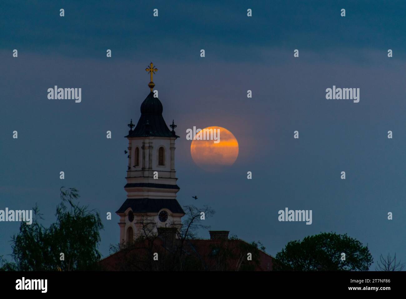 An illuminated full moon is gracefully setting behind a majestic ...