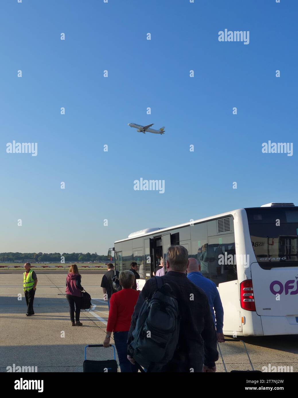 Airplane taking off as people board a shuttle bus at Gatwick airport ...