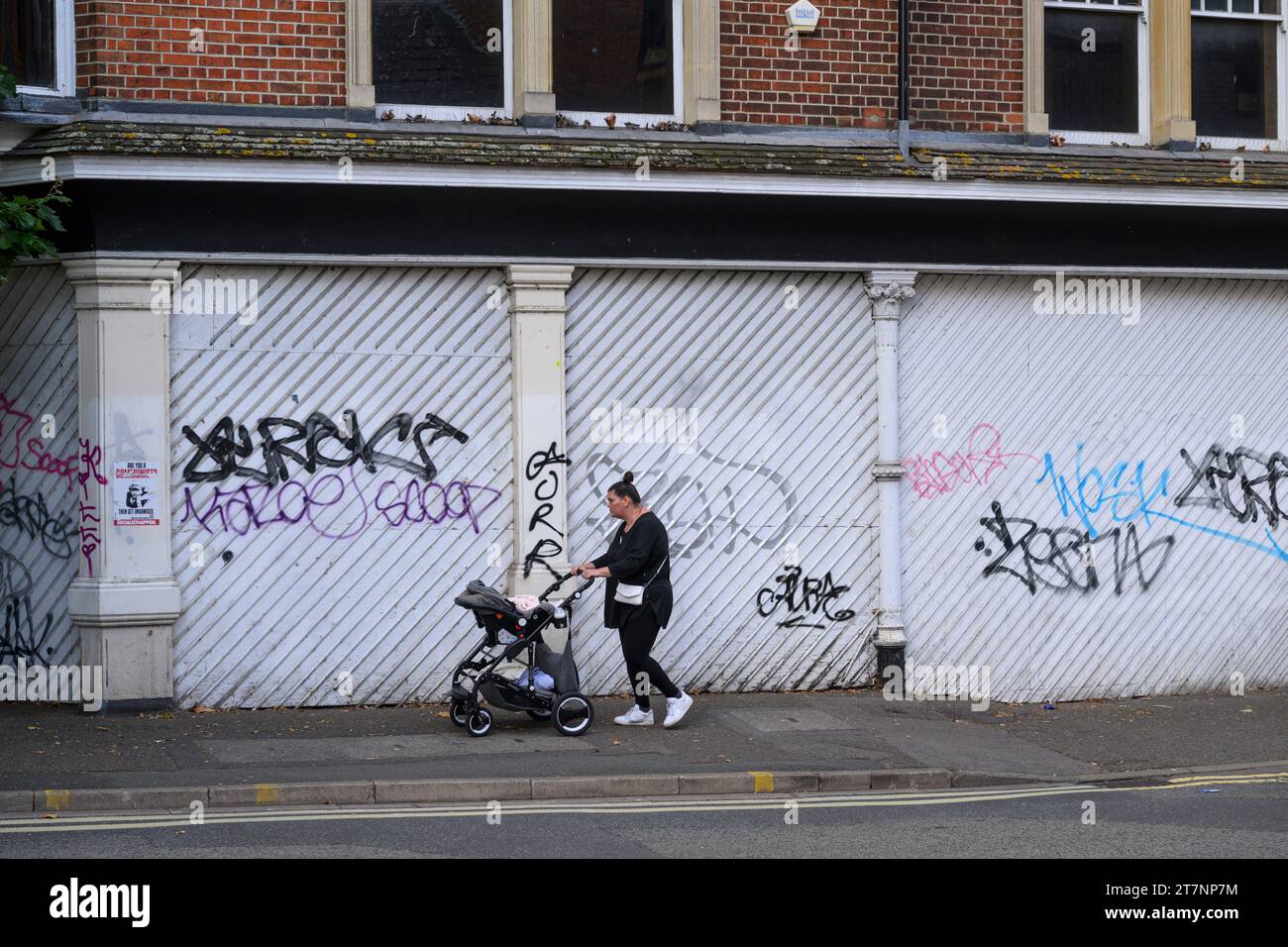 People walking closed down shop with its windows boarded up and covered ...