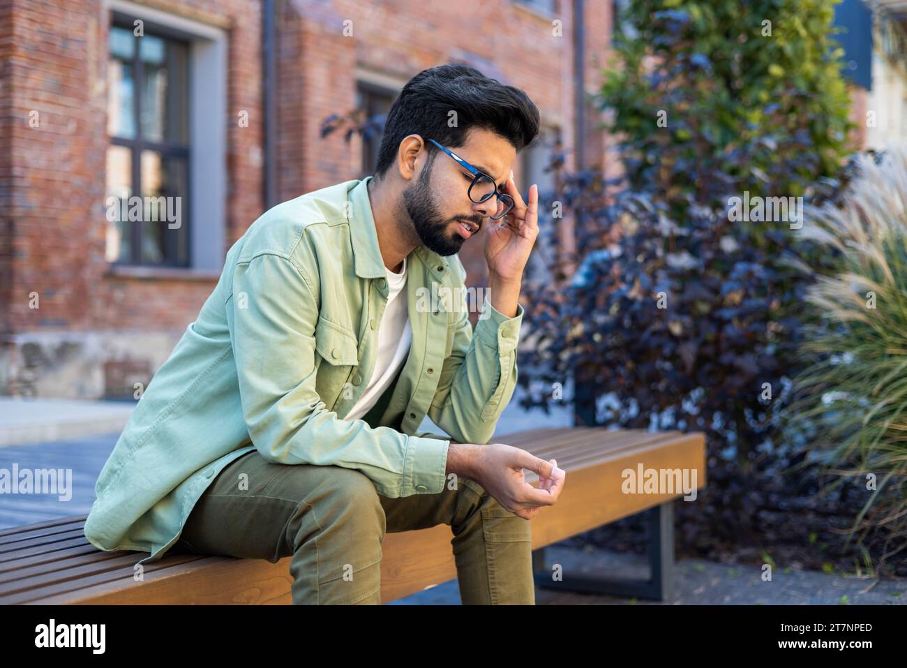 Sick man sitting on bench outside office building, Indian man having ...