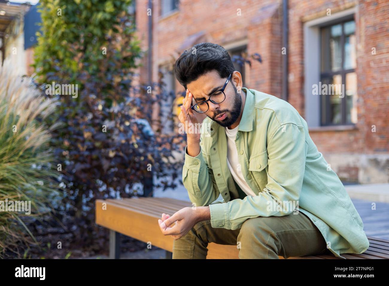 Sick man sitting on bench outside office building, Indian man having ...