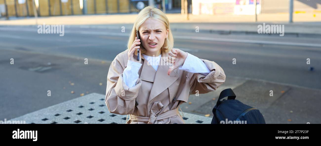 Disappointed young woman sitting on bench and showing thumbs down ...