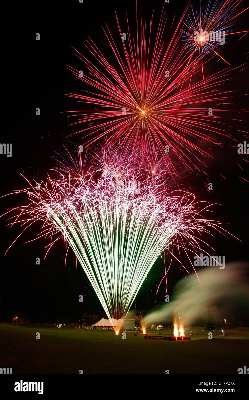 Colorful red, white, blue, pink and green aerial and ground fireworks explode in the night time ...