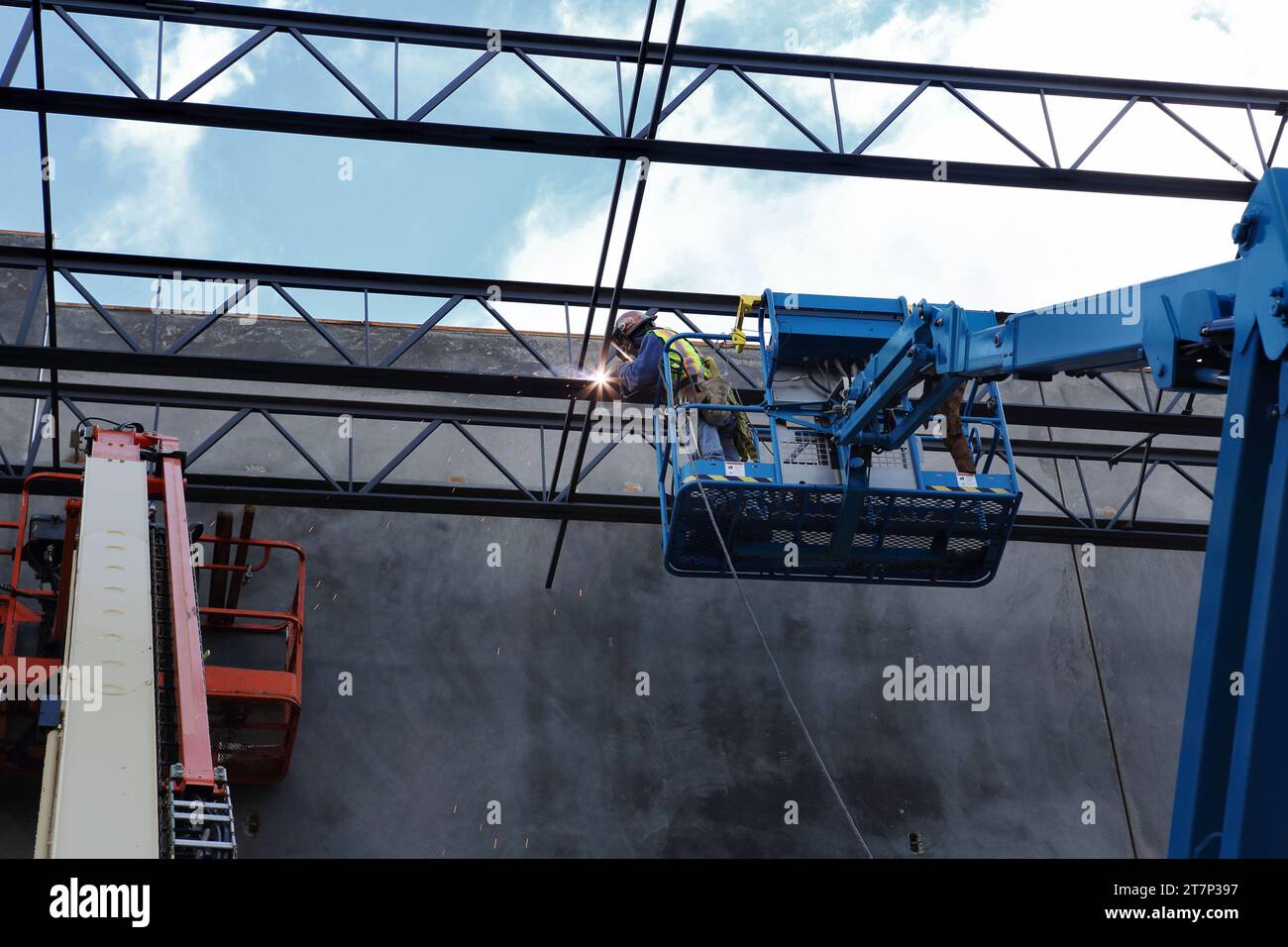 A welder welding steel roof trusses during the construction of a ...