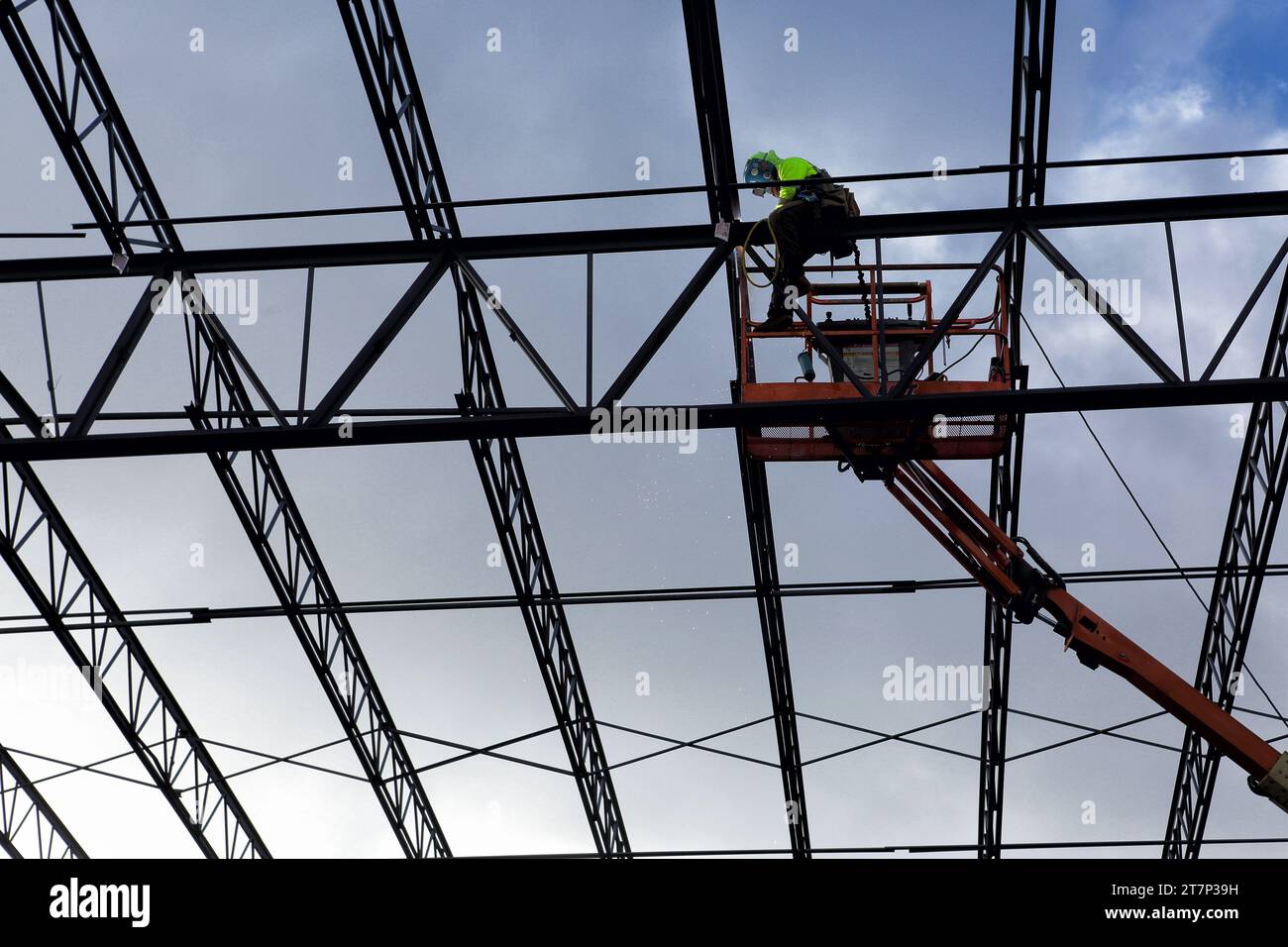 A welder welding steel roof trusses during the construction of a ...