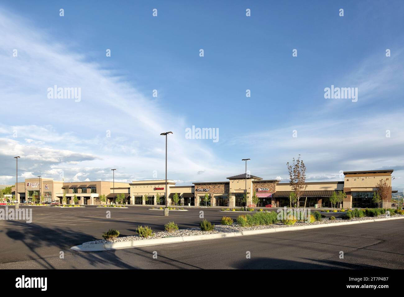 The exterior of a new modern strip mall, with empty parking lot, and a variety of store fronts ...