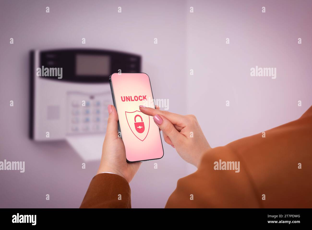 Woman operating home alarm system via mobile phone against white wall ...