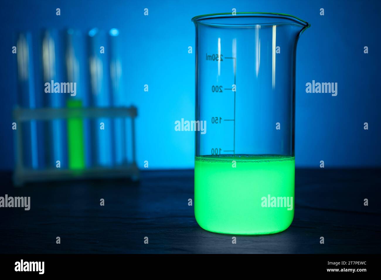 Laboratory beaker with luminous liquid on table against blue background ...