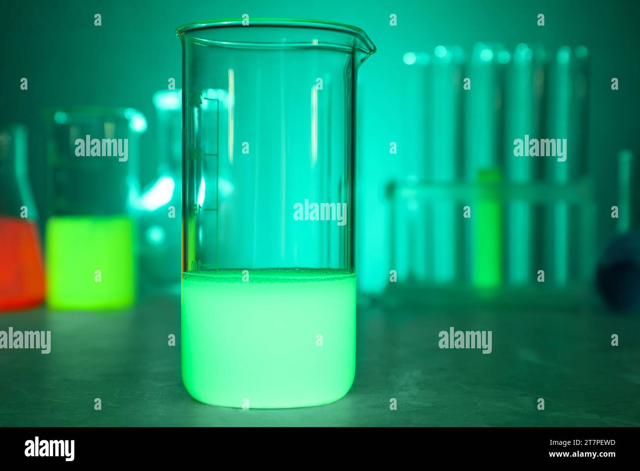 Laboratory beaker with luminous liquid on table against blurred ...
