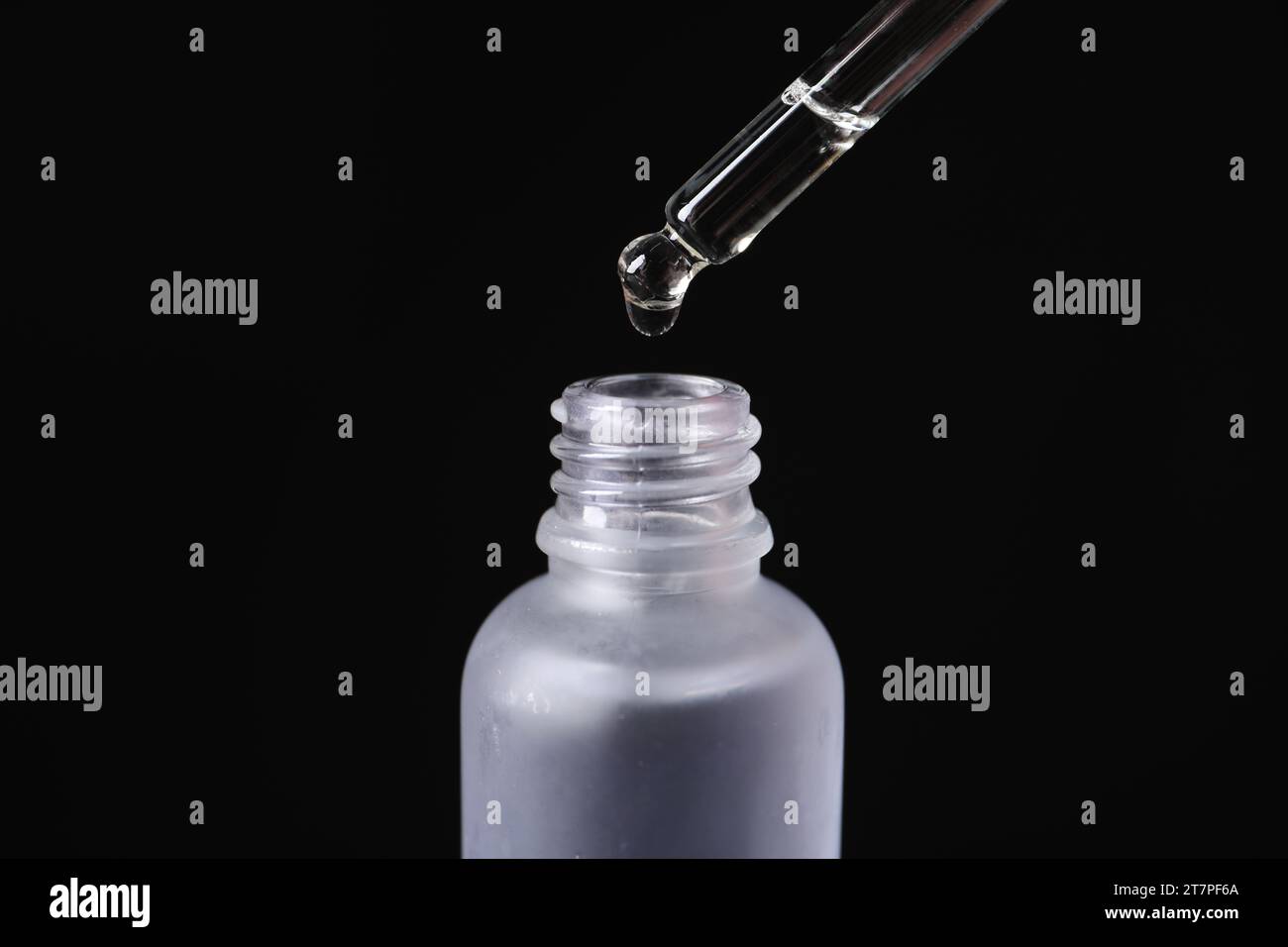 Dripping cosmetic serum from pipette into bottle on black background ...