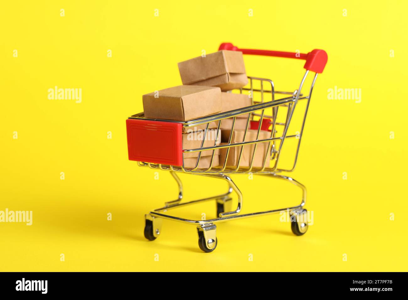 Small metal shopping cart with boxes on yellow background Stock Photo ...