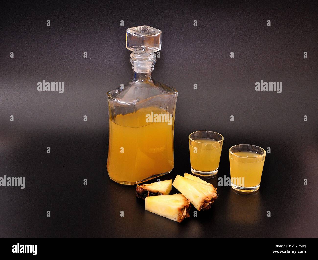Pineapple liqueur in two glasses and a bottle on a black background ...
