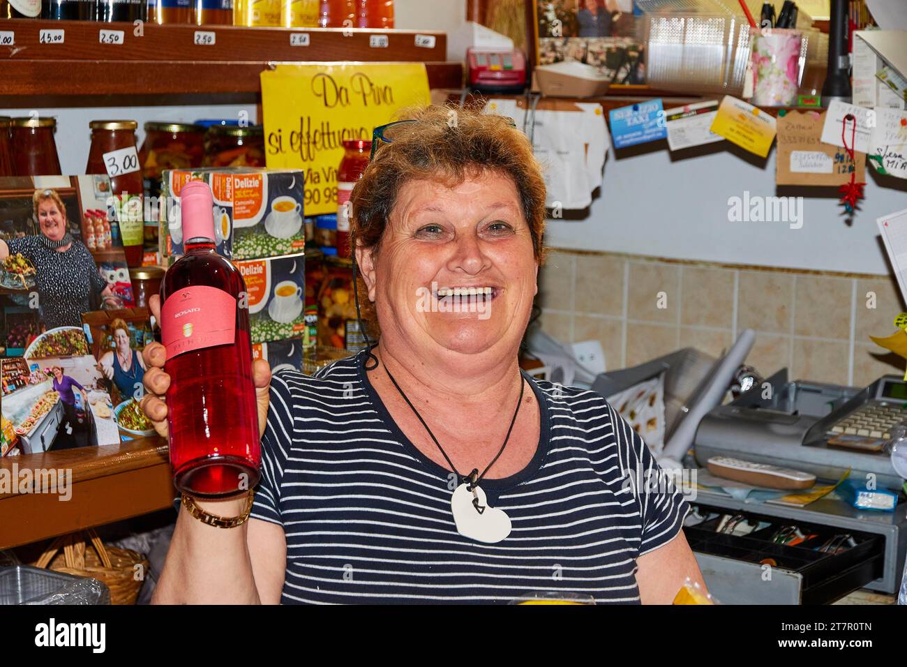 Owner, corner shop, holds up wine bottle, laughs, Lipari town, Lipari ...