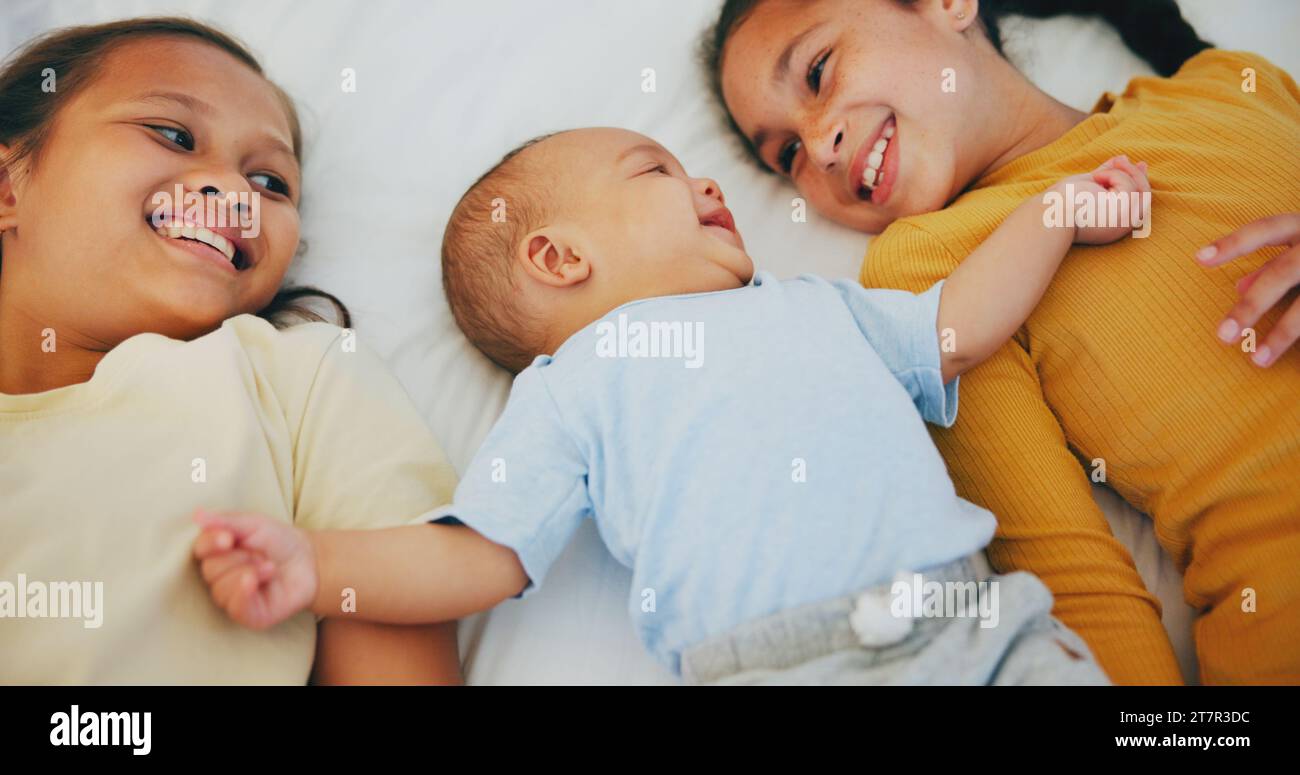 Love, family and sisters with baby boy on a bed for bonding, relax and conversation at home ...