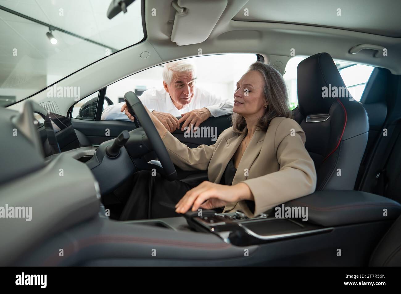 An elderly couple chooses a new car at a car dealership. Mature woman ...