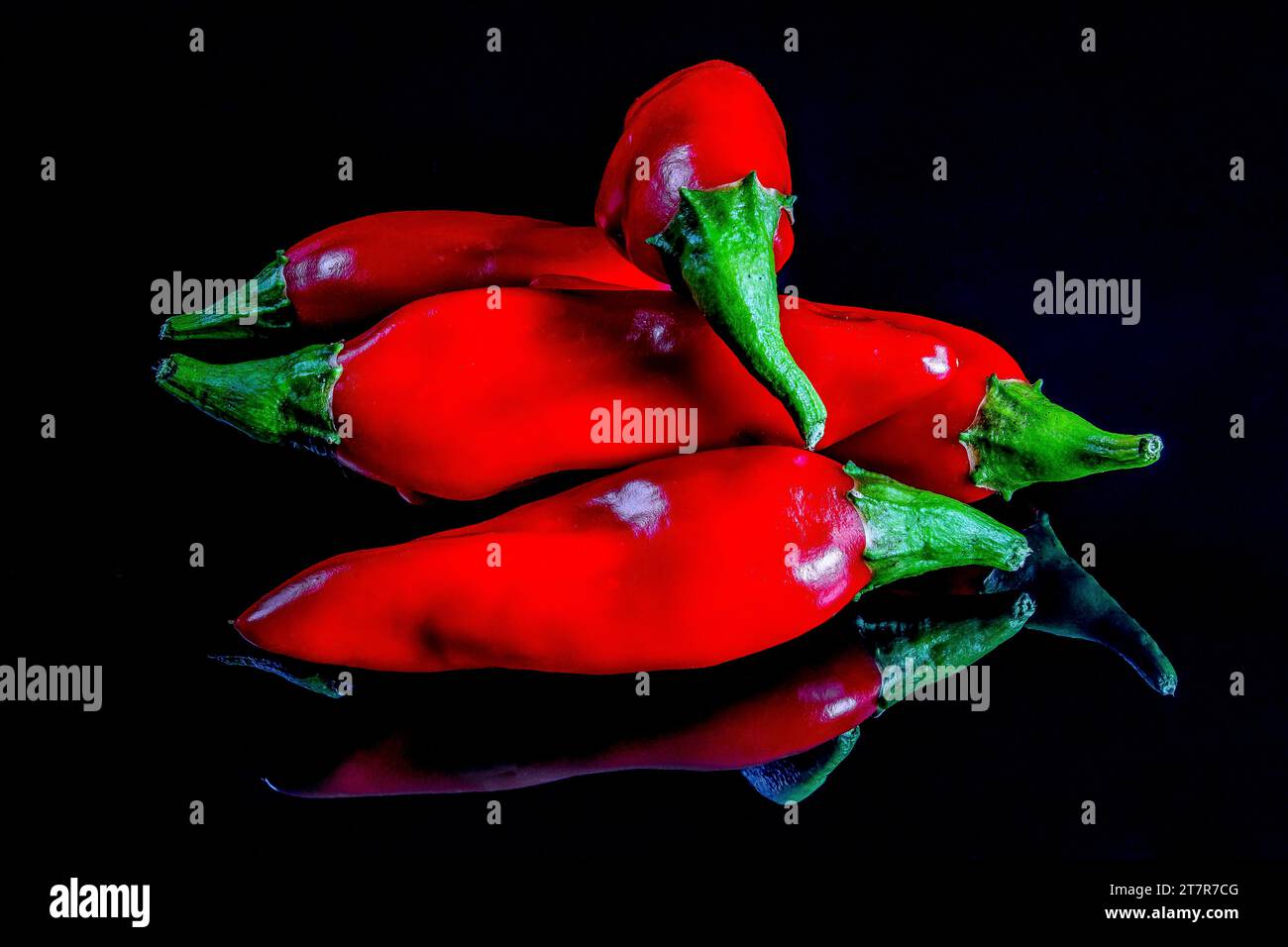 Five ripe red chili peppers isolated on a black reflecting background ...