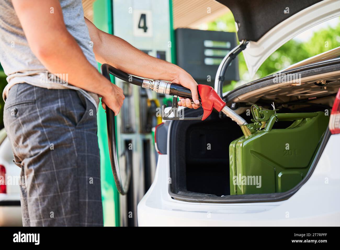 Male driver with gas pump refueling canister with fuel in car trunk ...