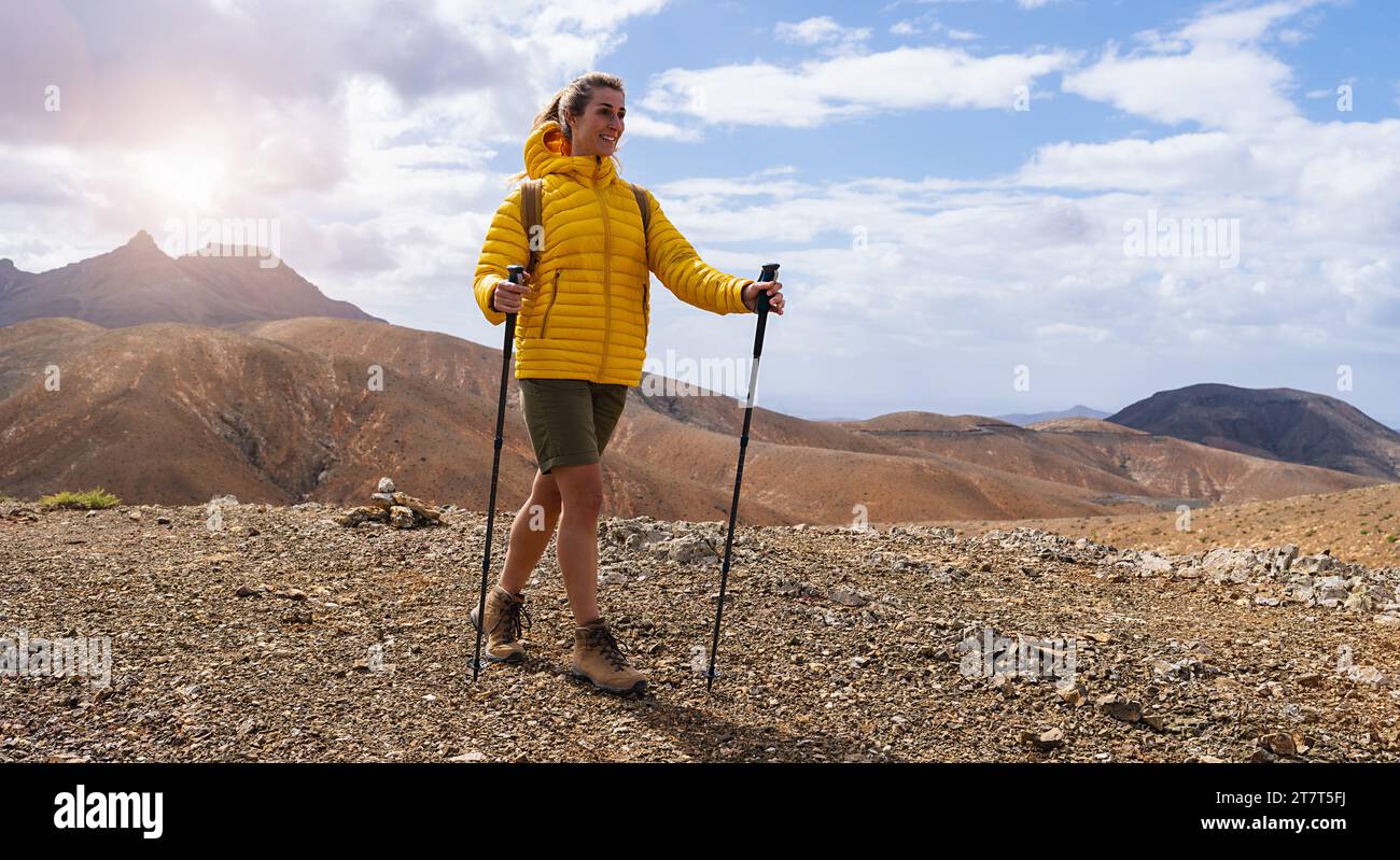 Hiker in yellow jacket with trekking poles on a mountain trail under a ...
