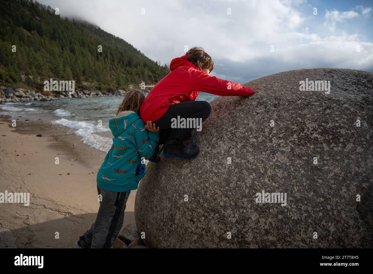 Sibling helping brother climb large boulder on shore of lake Stock Photo - Alamy