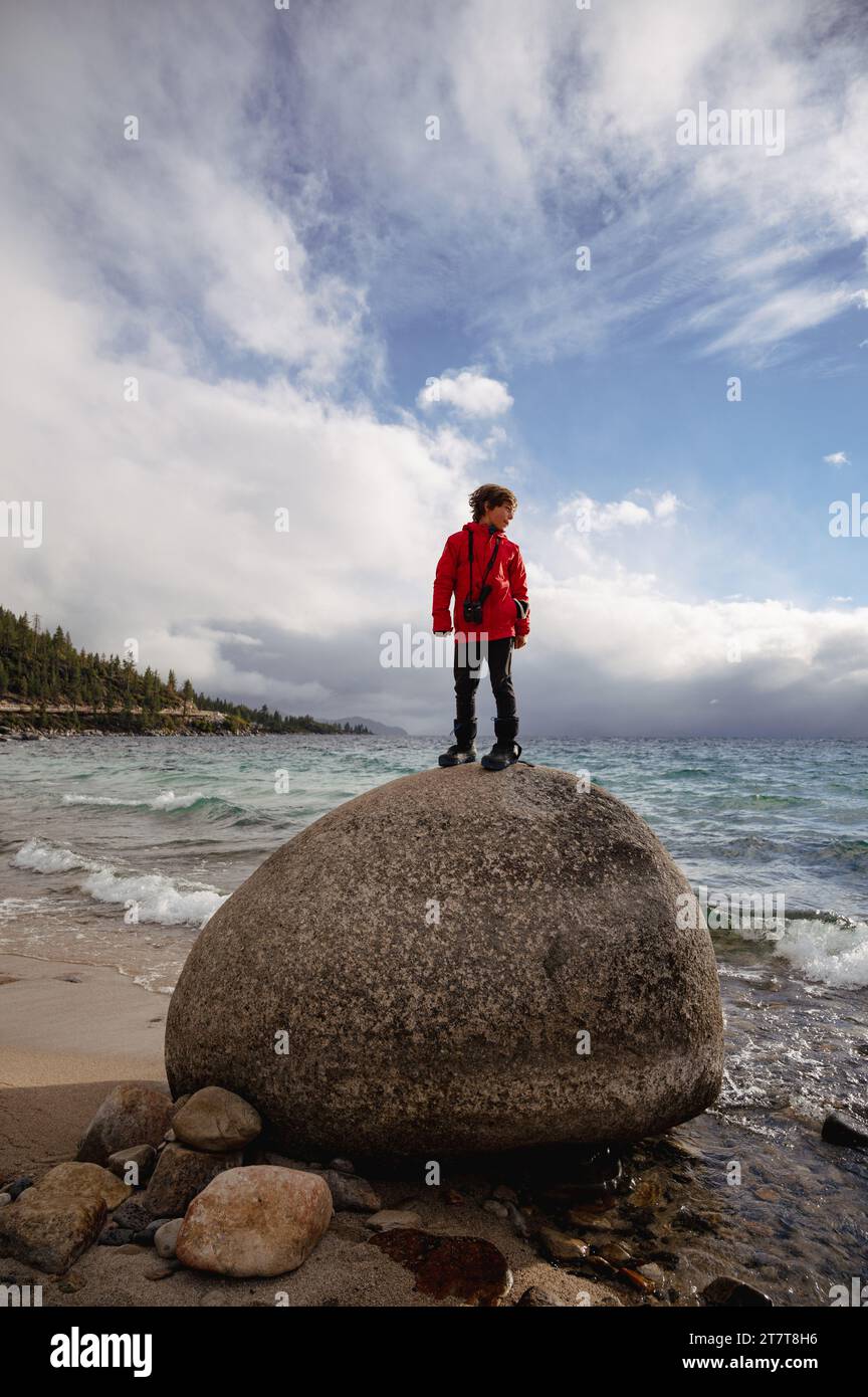 Boy in red standing on top of boulder on lakeshore looking out Stock ...