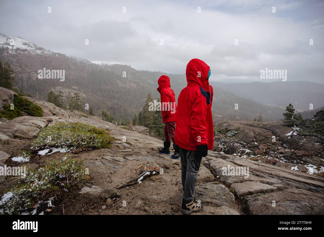 Two tweens in red coats look off into distance atop a mountain Stock ...